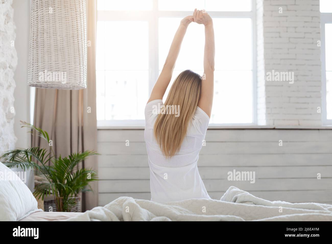 Well-rested blonde woman enjoying happy morning, stretching in bed ...