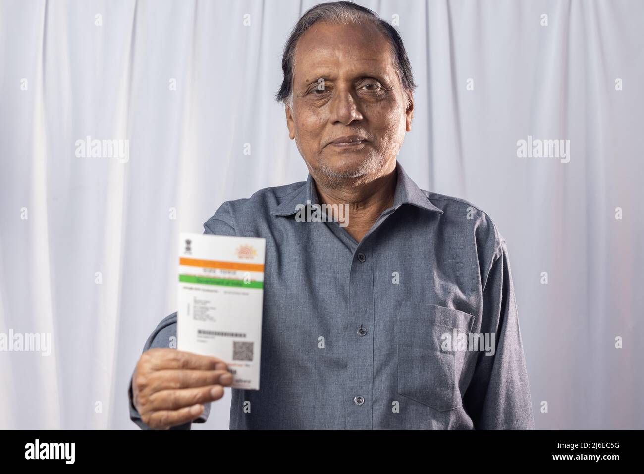 An Indian old man smiling with Aadhaar card in hands on white ...