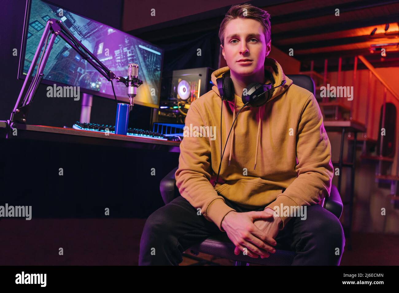 Smiling pro gamer sitting by equipment for gaming and live streaming at ...