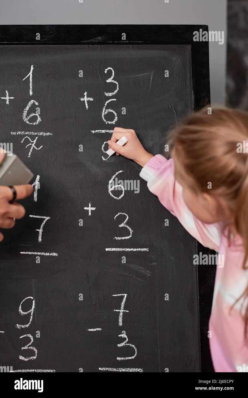 Girl writing down math solution on blackboard while counting numbers at ...