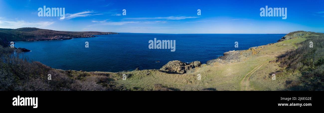 Panorama of a wild stone and sandy beach with dark wet sea sand and ...