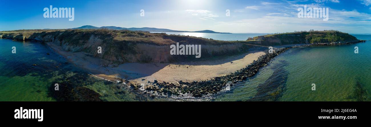 Panorama of a wild stone and sandy beach with dark wet sea sand and ...