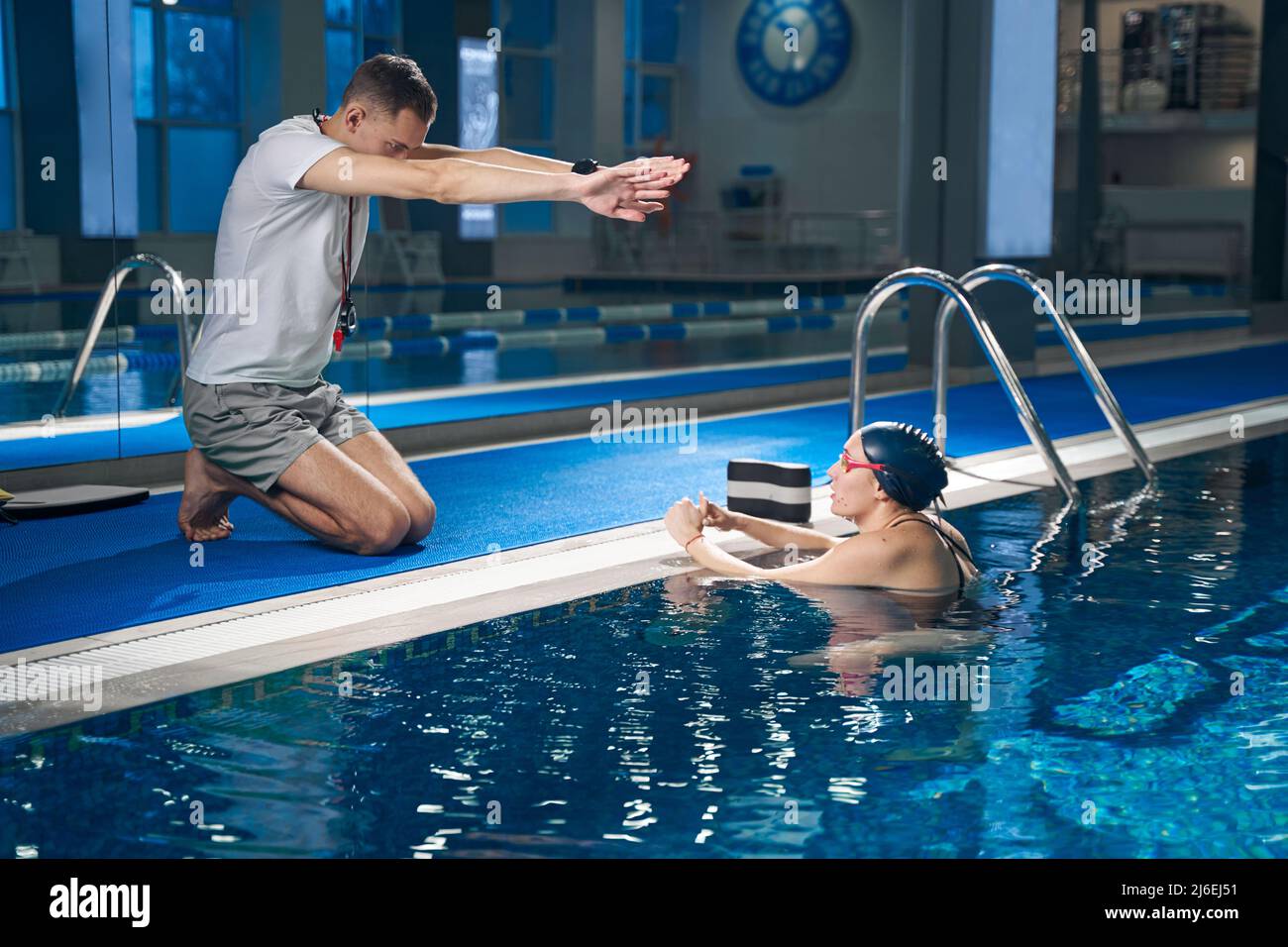 Caucasian coach near the swimming pool showing the exercise to the ...