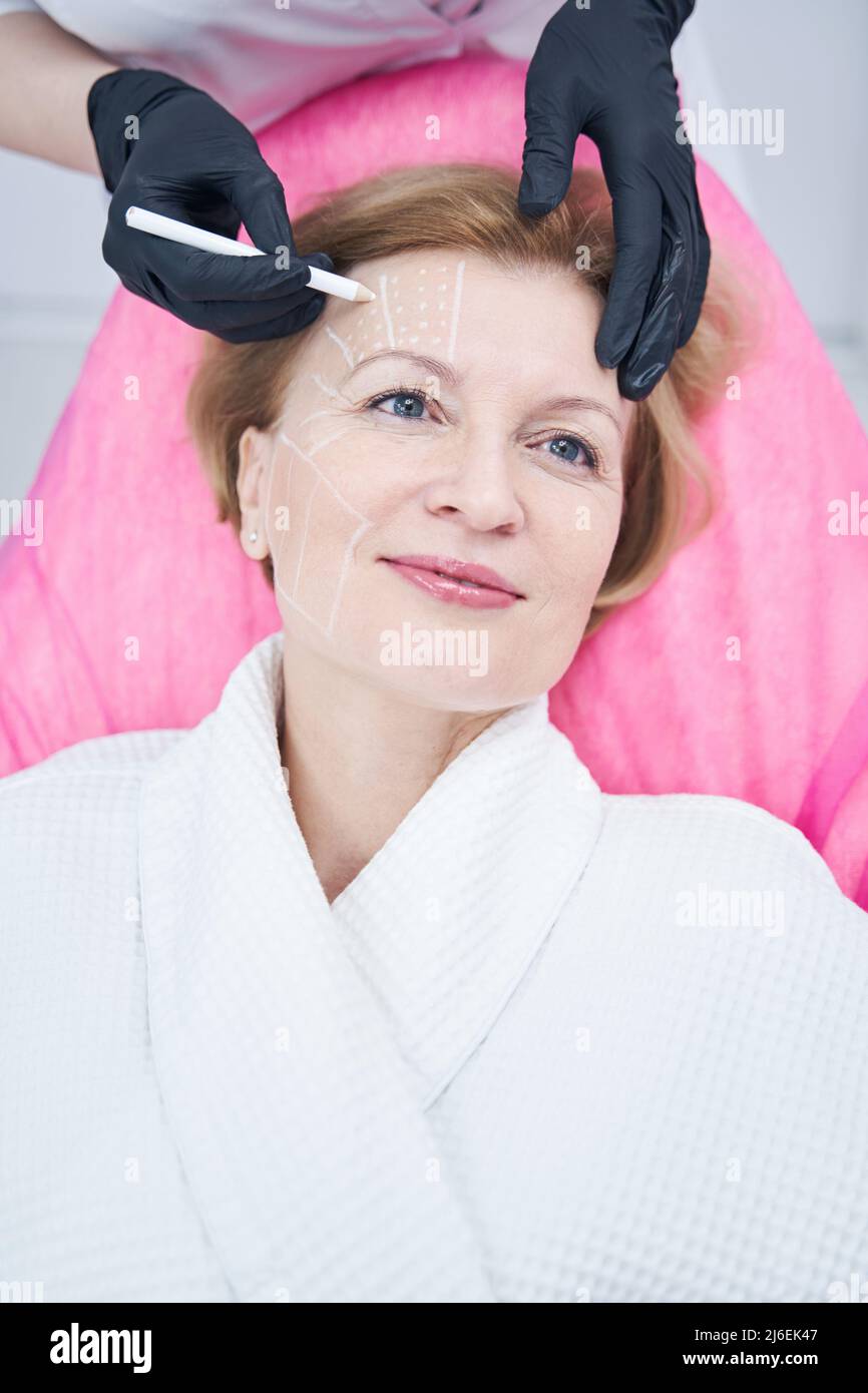 Cosmetologist drawing marks on woman forehead in beauty salon Stock ...