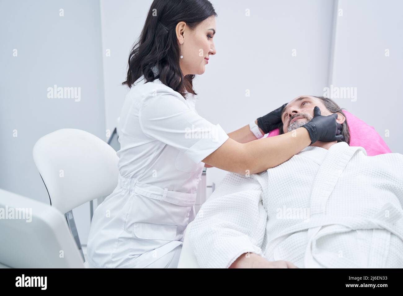 Positive delighted cosmetologist checking male skin on face Stock Photo ...