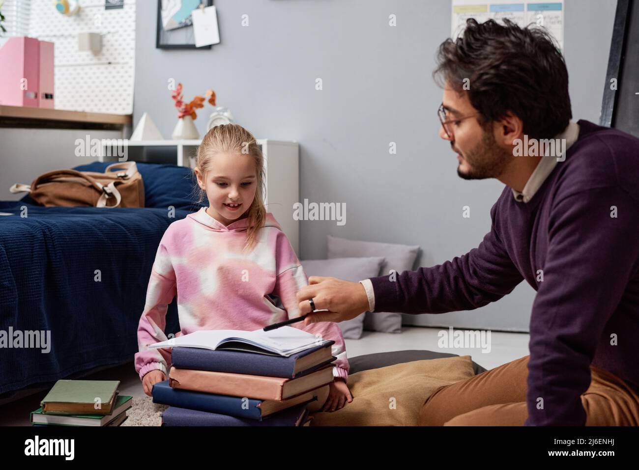 Serious young middle eastern tutor pointing at workbook on stack of ...