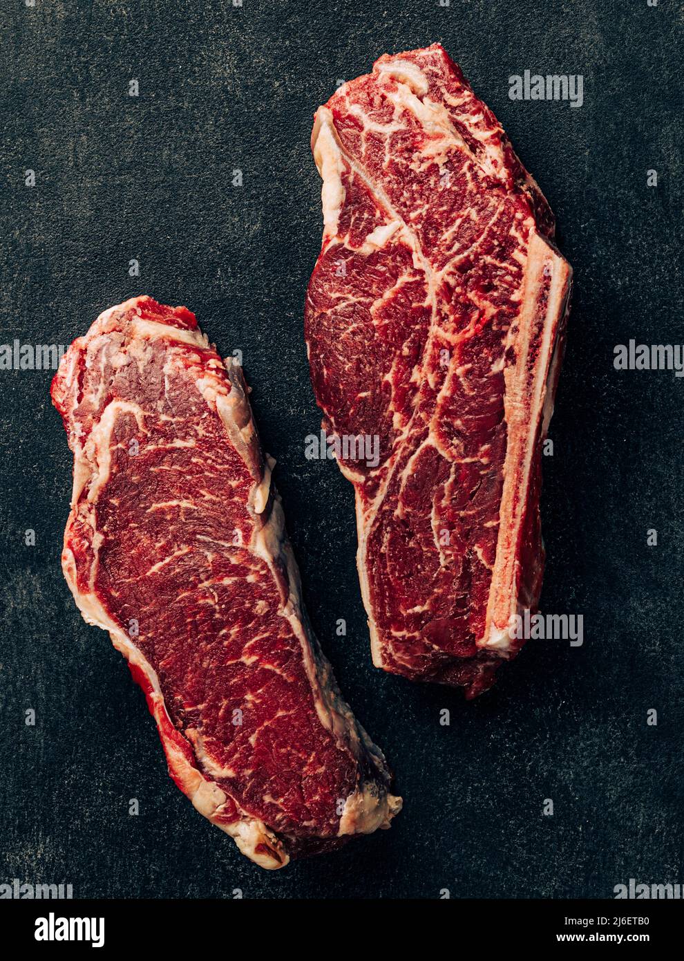 Two boneless and striploin on bone steak on black stone table. Top view ...