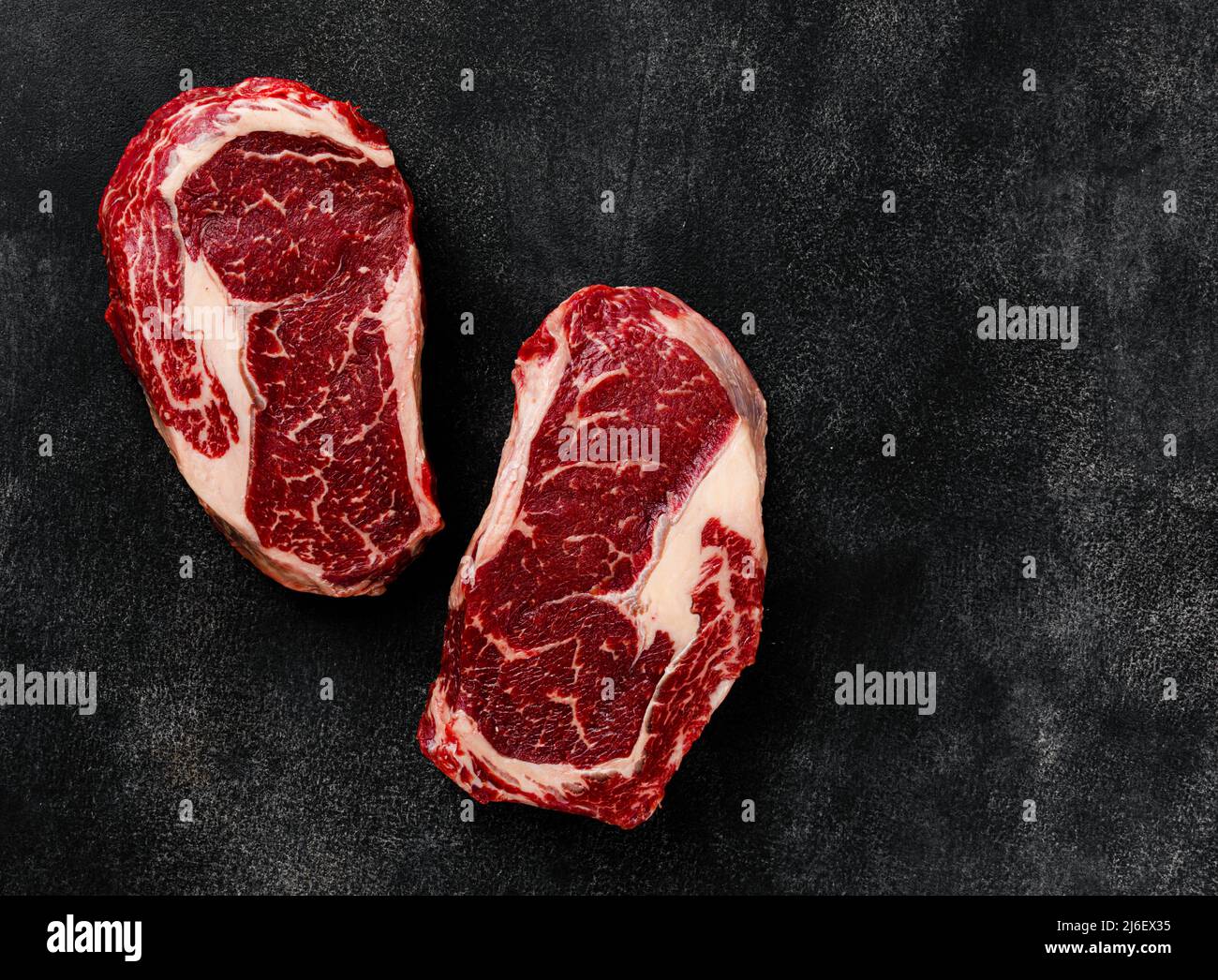 Ribeye raw meat beef steak. Top view over black stone background Stock ...