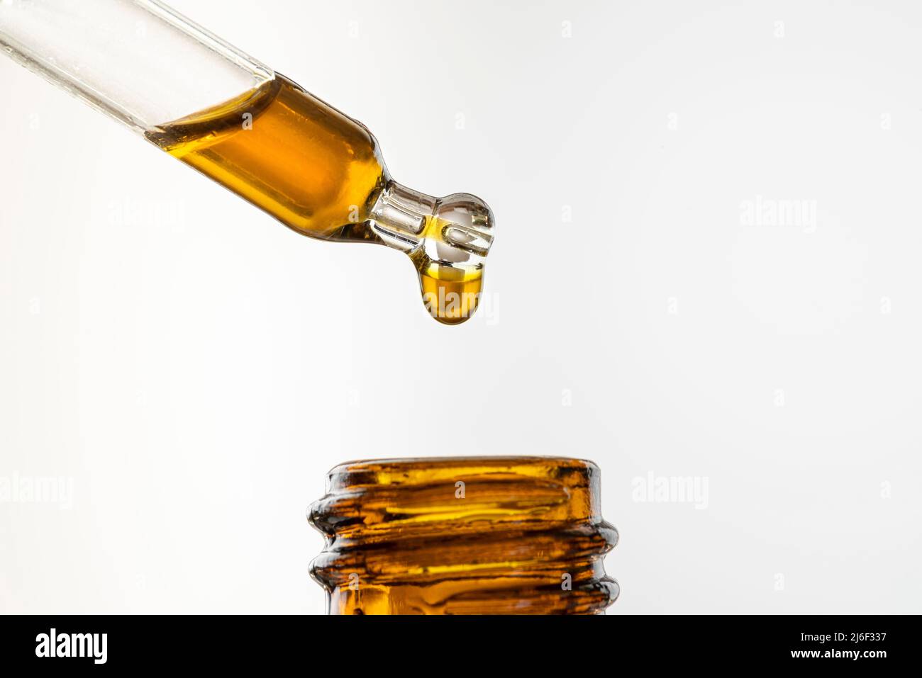 Pipette of orange-yellow essential oil, with a drop on top of a bottle ...
