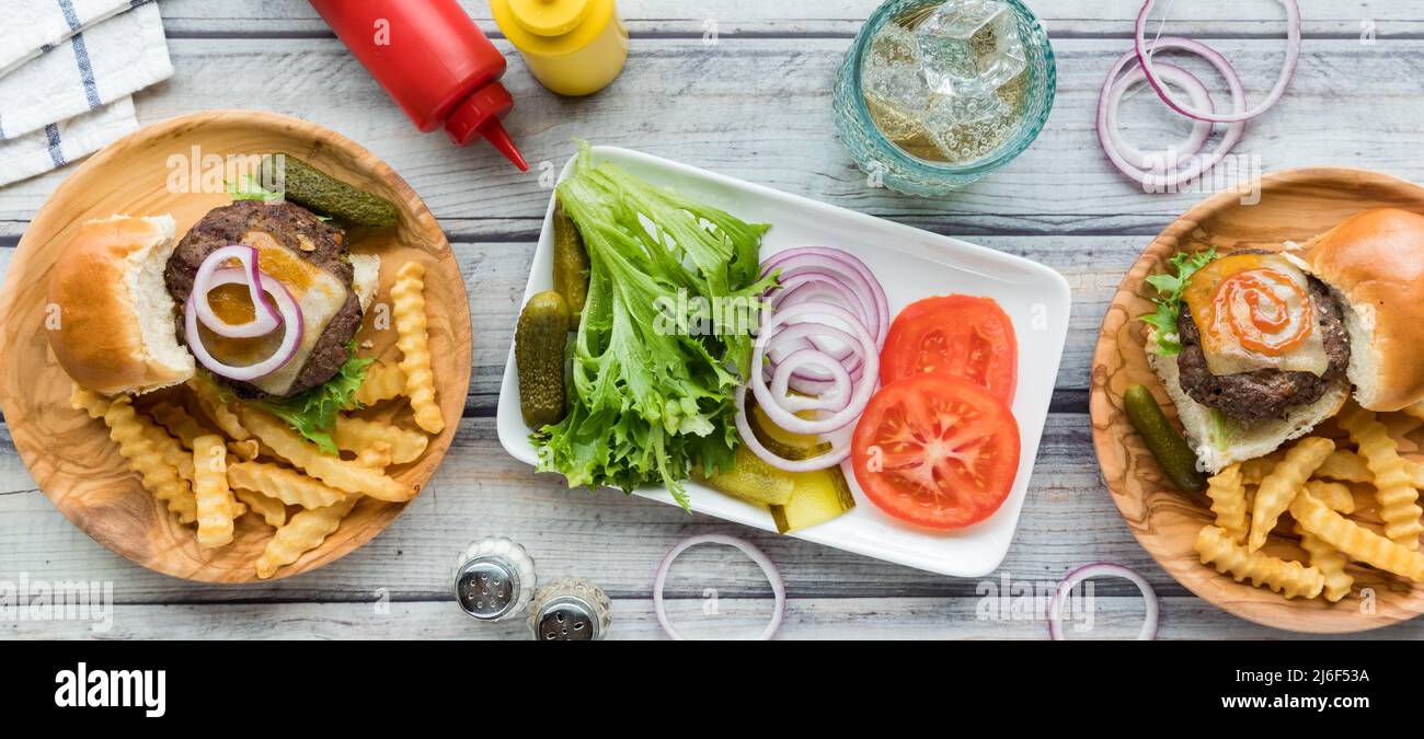 A narrow view of cheeseburger sliders with a platter of toppings in the ...