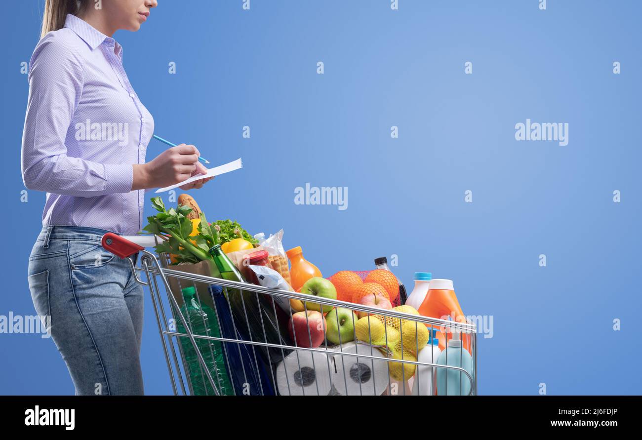 Woman checking a shopping list and trolley full of fresh goods, grocery ...