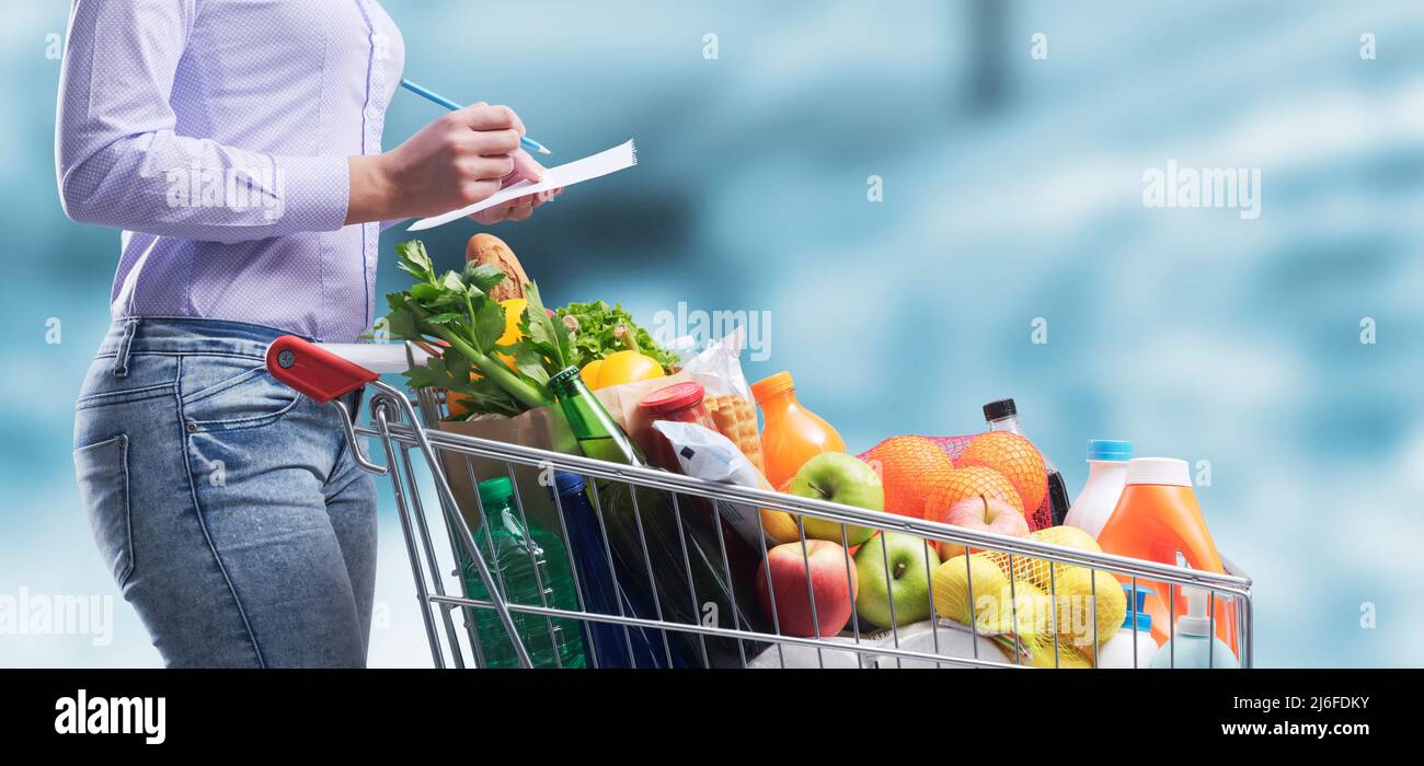 Woman writing a shopping list and buying goods at the supermarket, her ...