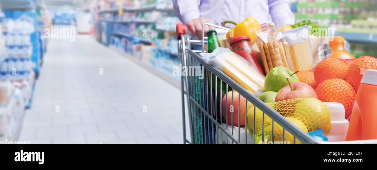 Woman pushing a full trolley at the supermarket, grocery shopping ...