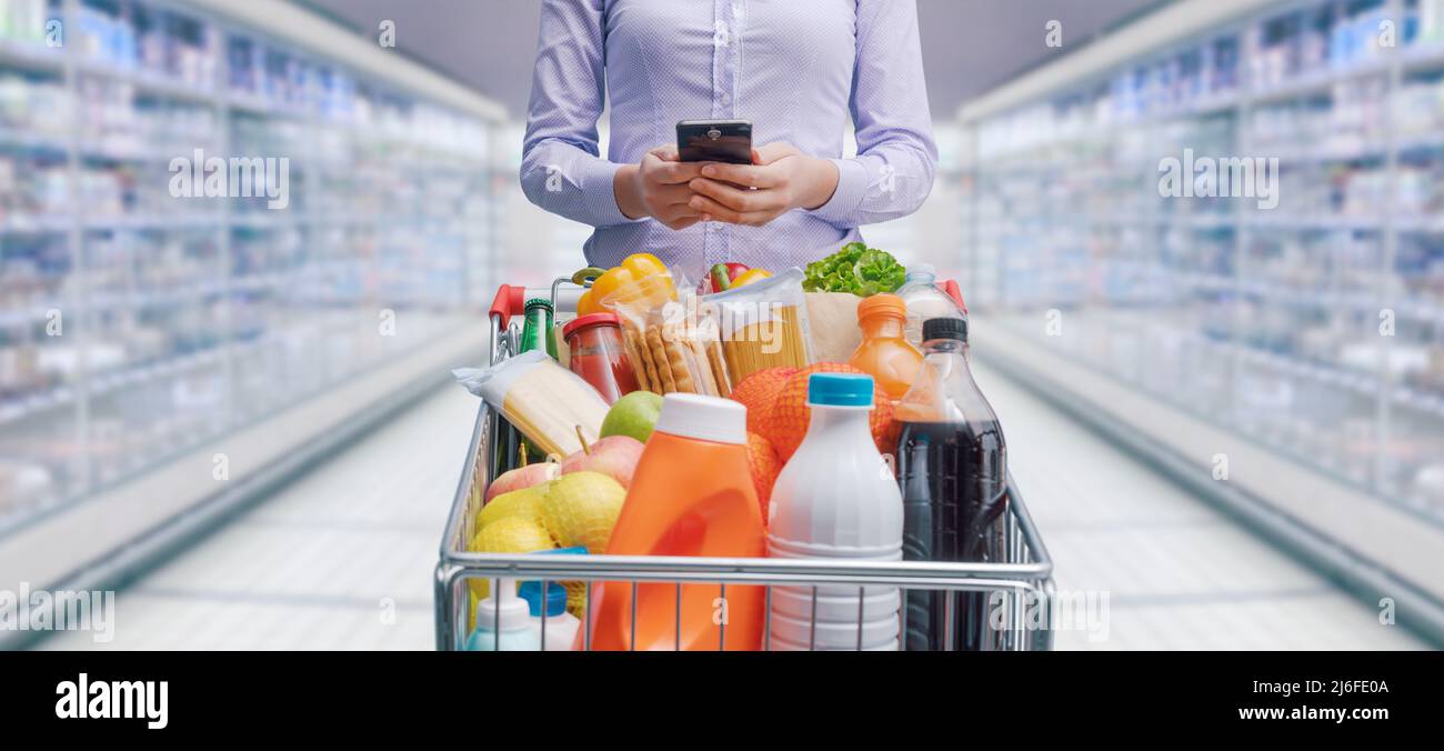 Woman doing grocery shopping at the supermarket, she is using apps on ...