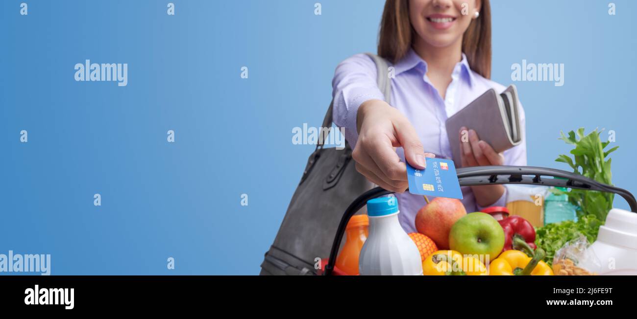 Woman holding a full shopping basket and paying for groceries using a ...