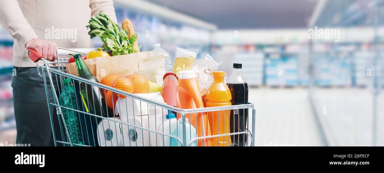 Man pushing a full trolley at the supermarket, grocery shopping concept ...