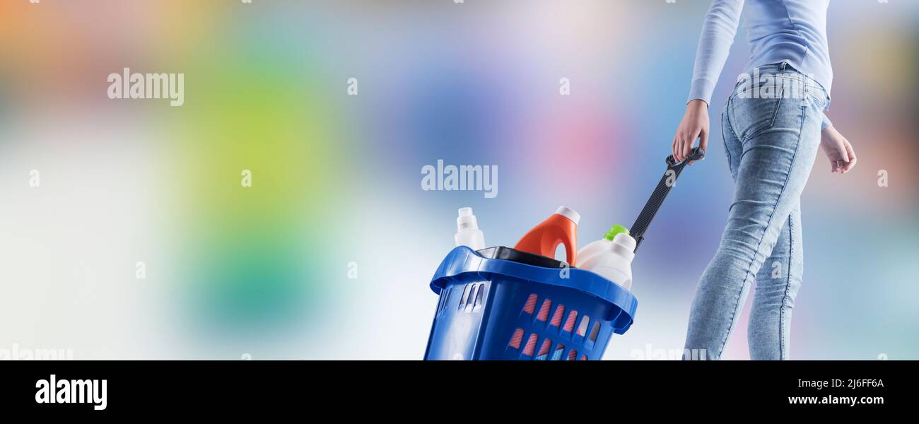 Woman pulling a shopping basket full of cleaning products, blank copy ...