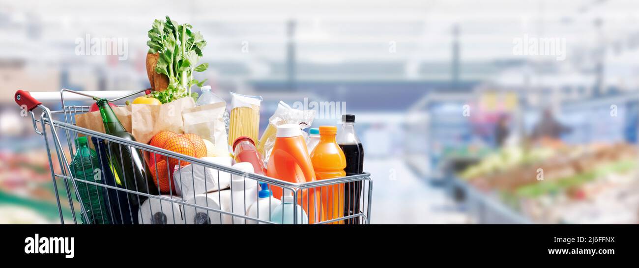 Shopping cart filled with food and drinks and supermarket shelves in ...