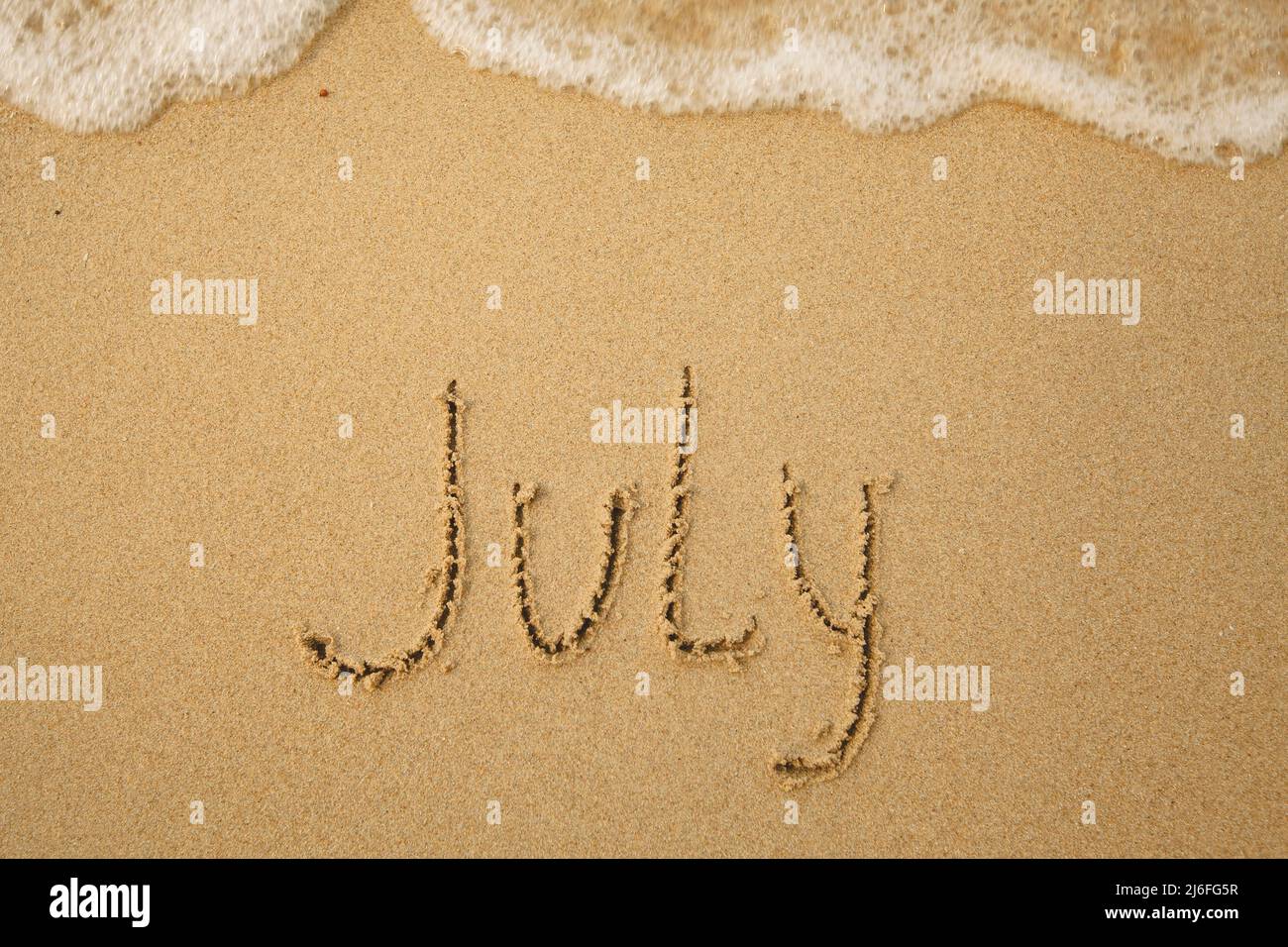 July - handwritten on the soft beach sand Stock Photo - Alamy