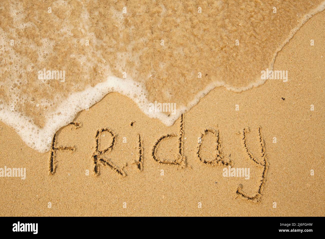 Friday - handwritten on the light beach sand with a soft wave lapping ...