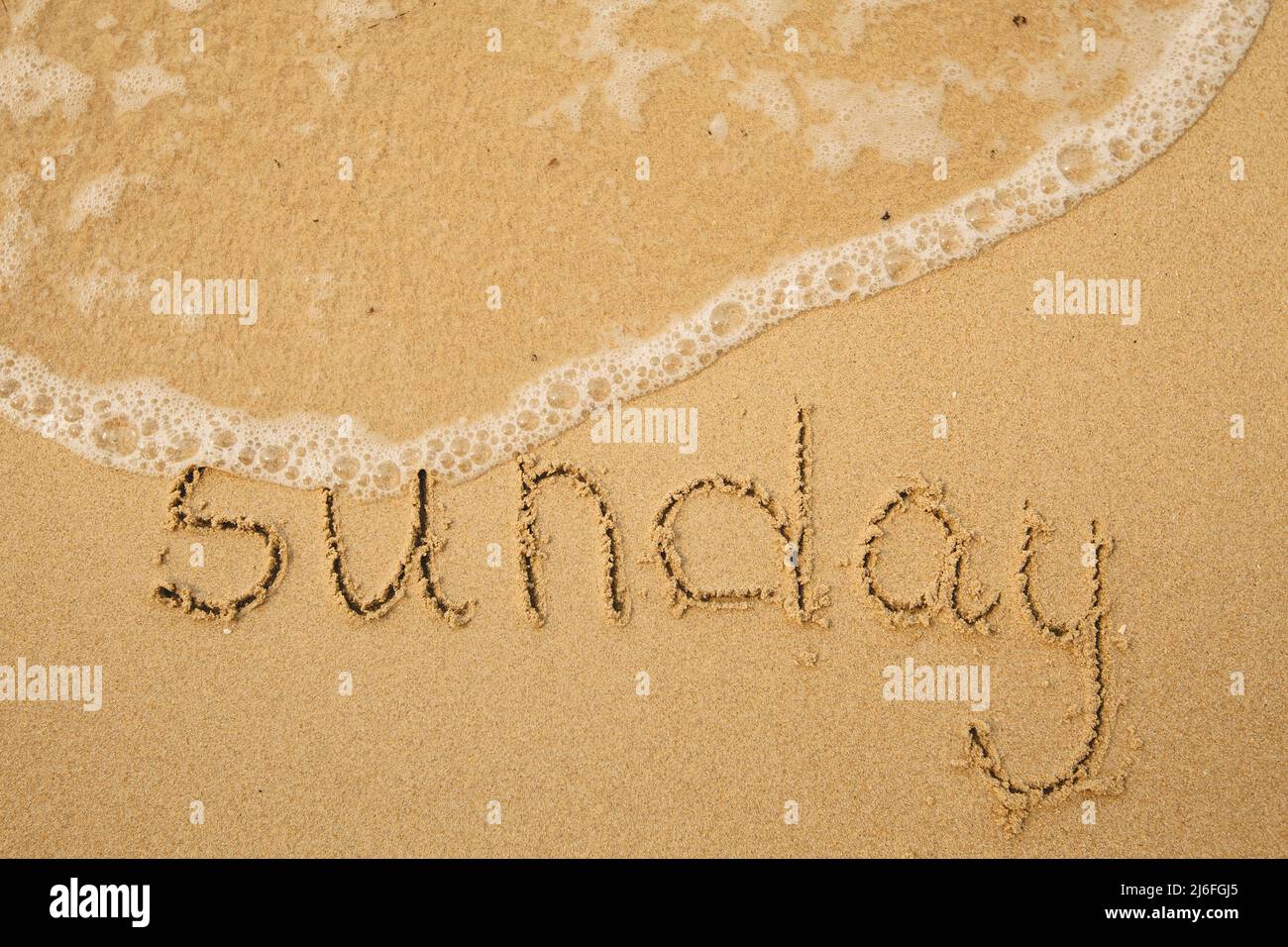 Sunday - handwritten on the light beach sand with a soft wave lapping ...