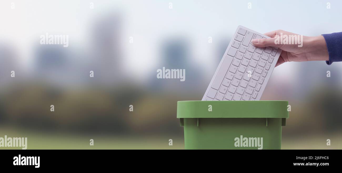 Woman putting a computer keyboard in the trash bin, e-waste recycling ...