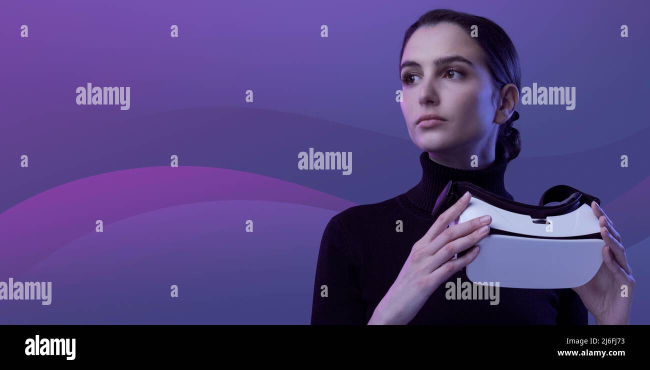 Attractive young woman holding a VR headset and looking away, virtual ...