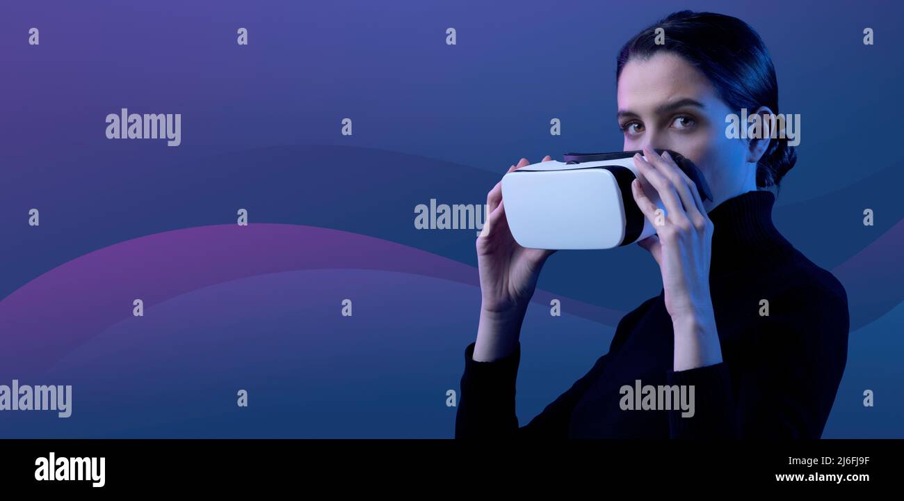 Attractive woman looking at camera and holding a VR headset in front of ...