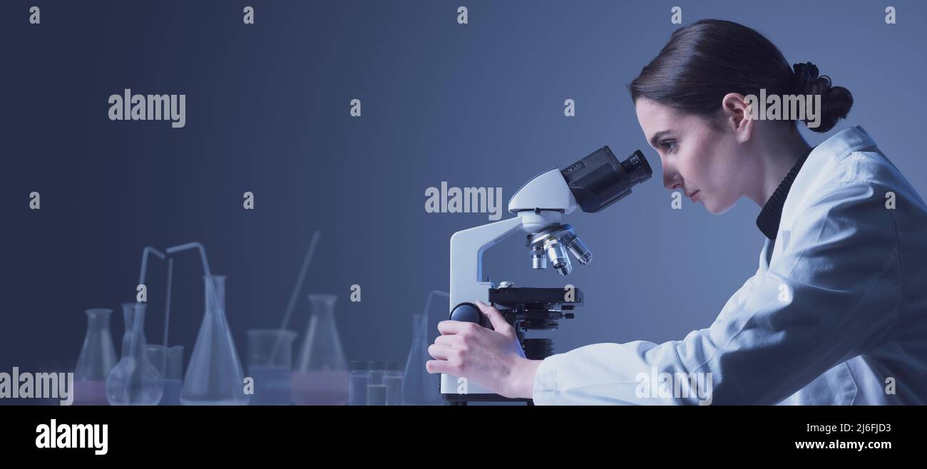 Young researcher working in the lab, she is looking through a ...