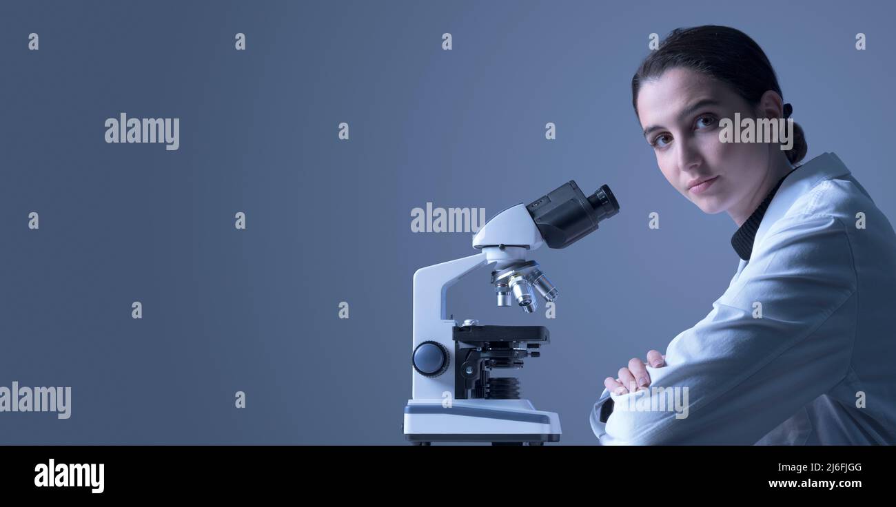 Young female researcher using a microscope and looking at camera ...
