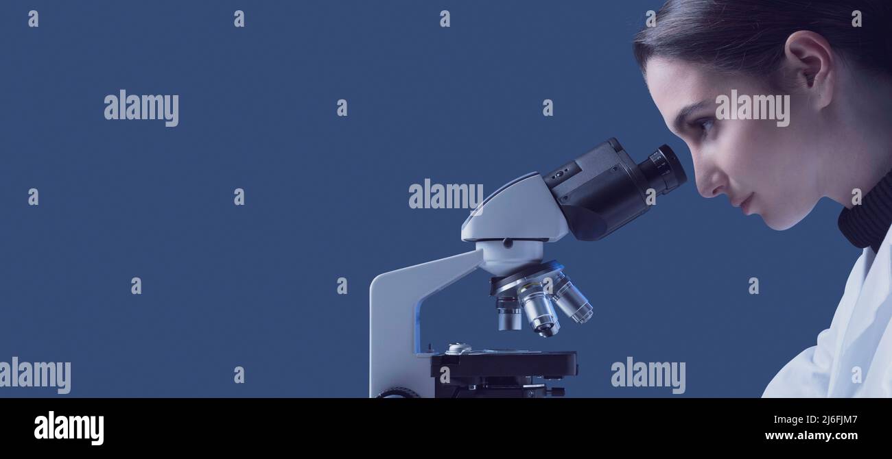 Young researcher looking through a microscope and checking samples ...