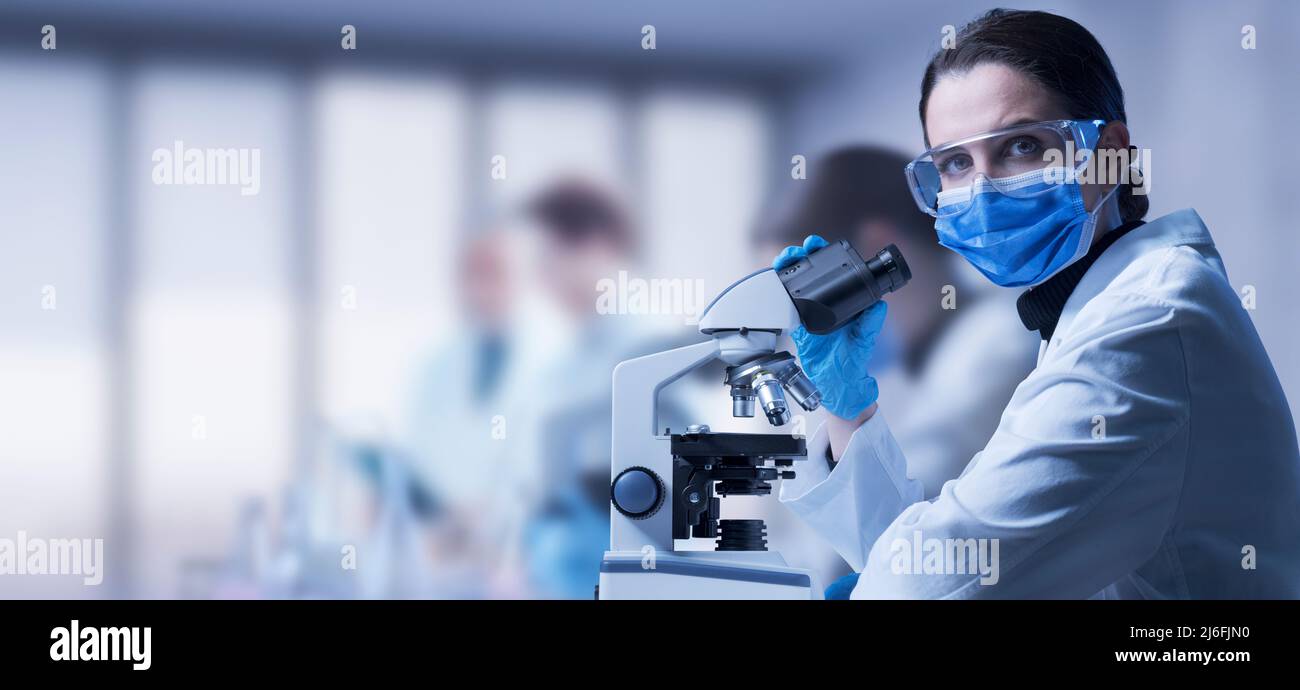 Researcher wearing a surgical mask and using a microscope, she is ...