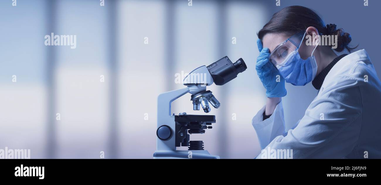 Pensive disappointed researcher with face mask in the lab, she is using ...