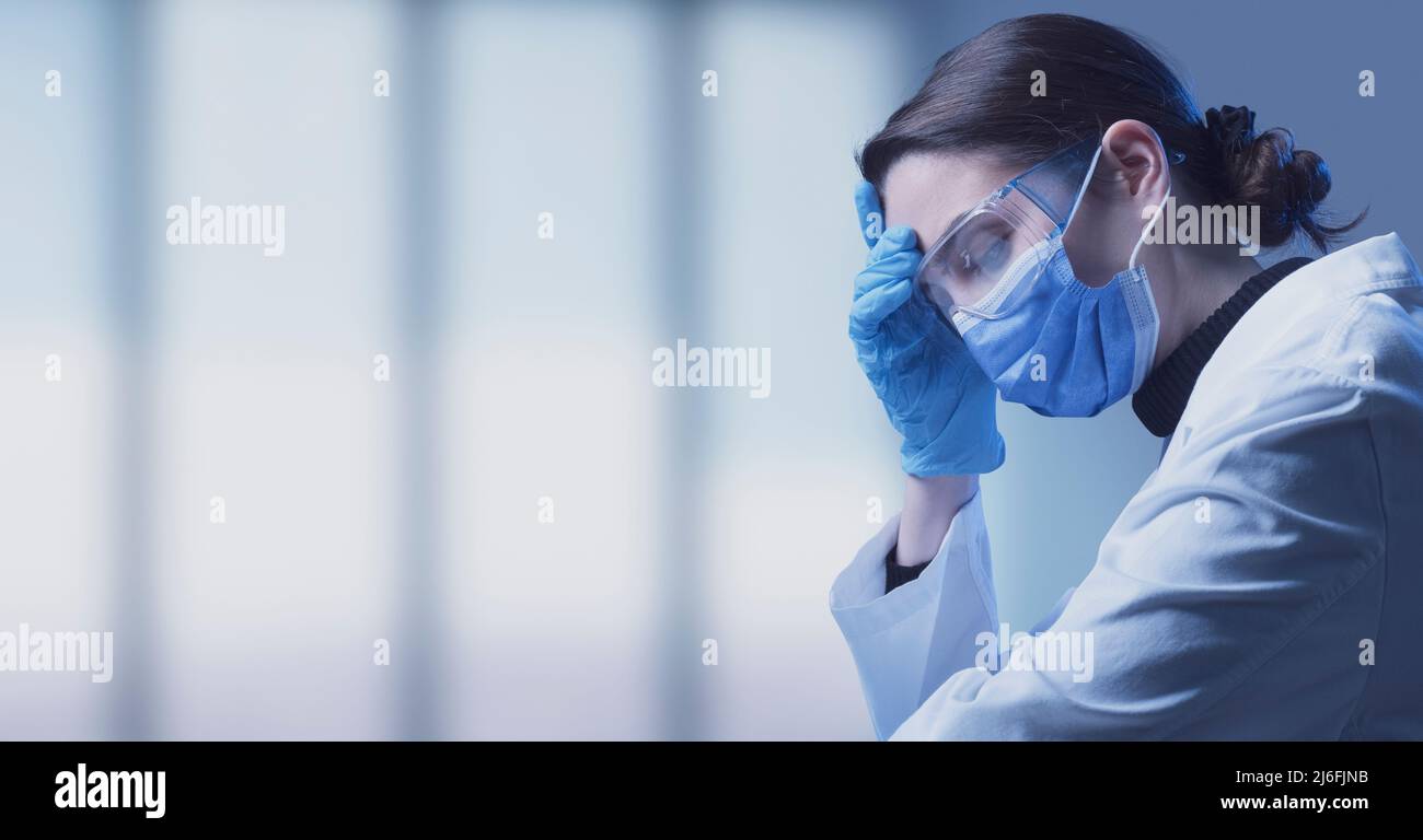 Pensive researcher wearing a face mask and touching her head, medical ...