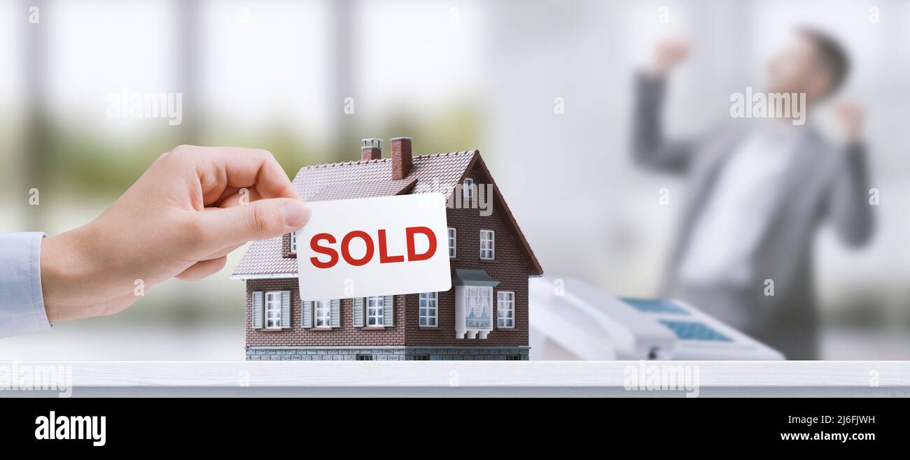 Real estate agent holding a sold sign in front of a model house ...