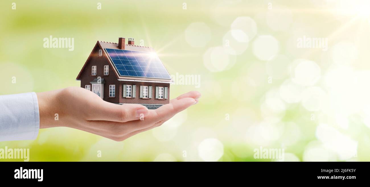 Hand holding an energy efficient model house with solar panels, ecology ...