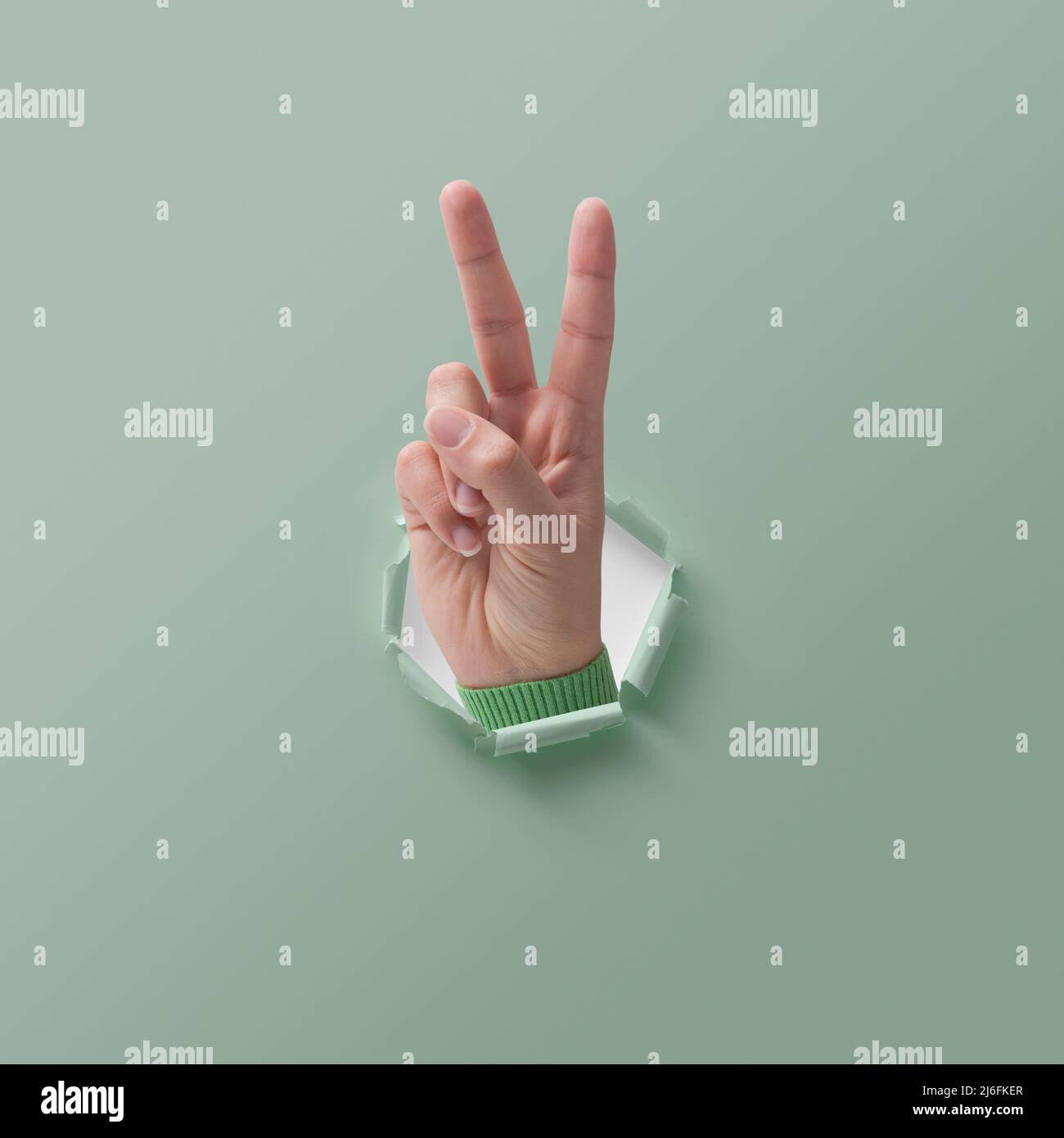 Woman showing V-sign through torn paper, victory and peace concept ...