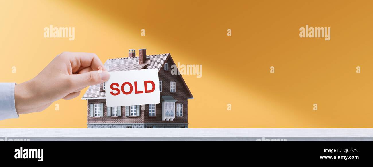 Real estate agent holding a sold sign in front of a model house ...
