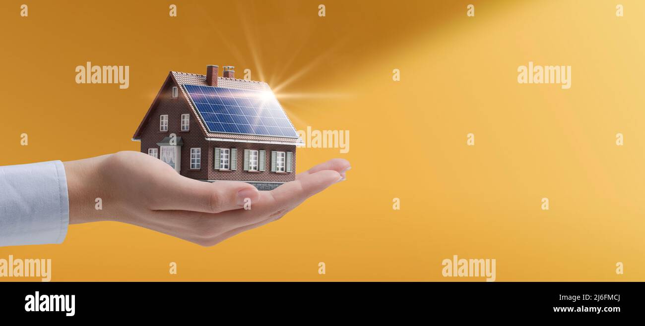 Hand holding an energy efficient model house with solar panels, ecology ...