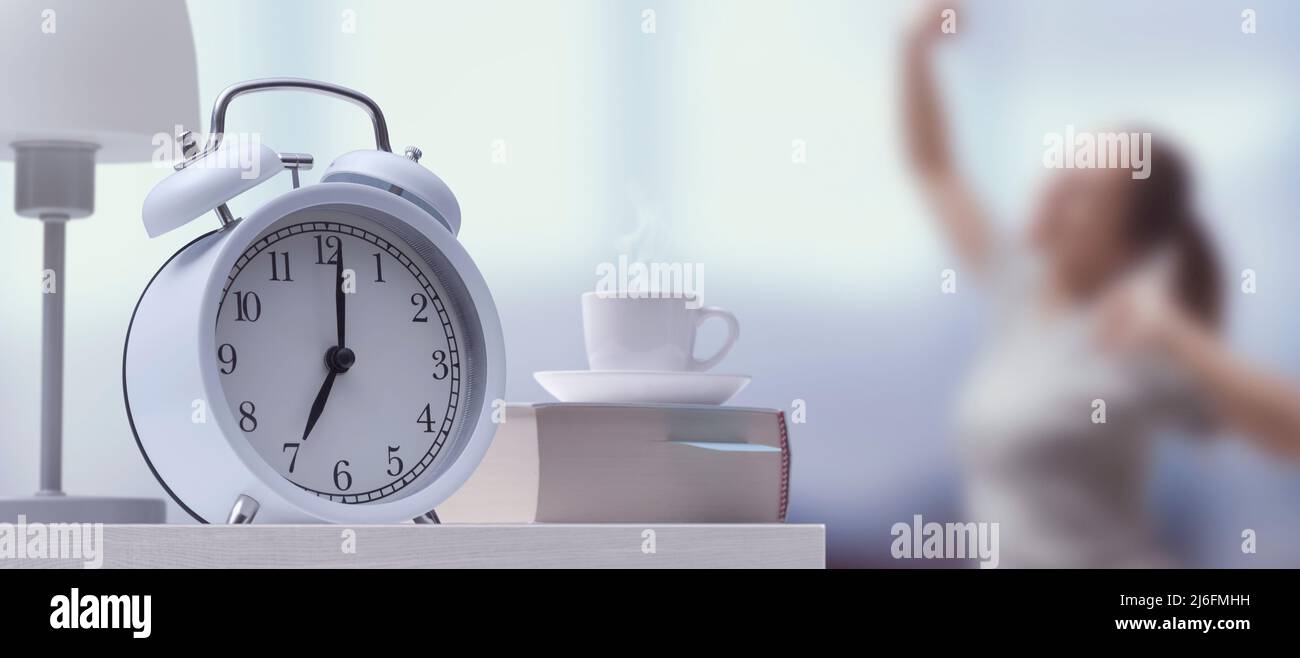 Alarm clock on the bedside table, a woman is getting up and stretching ...