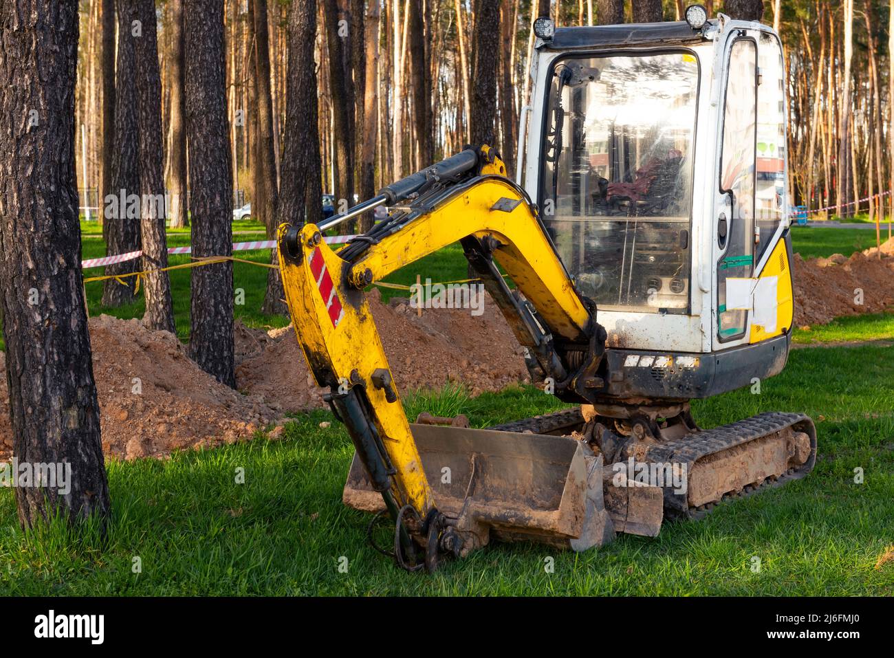 A small excavator digs a trench in the forest for power wires ...