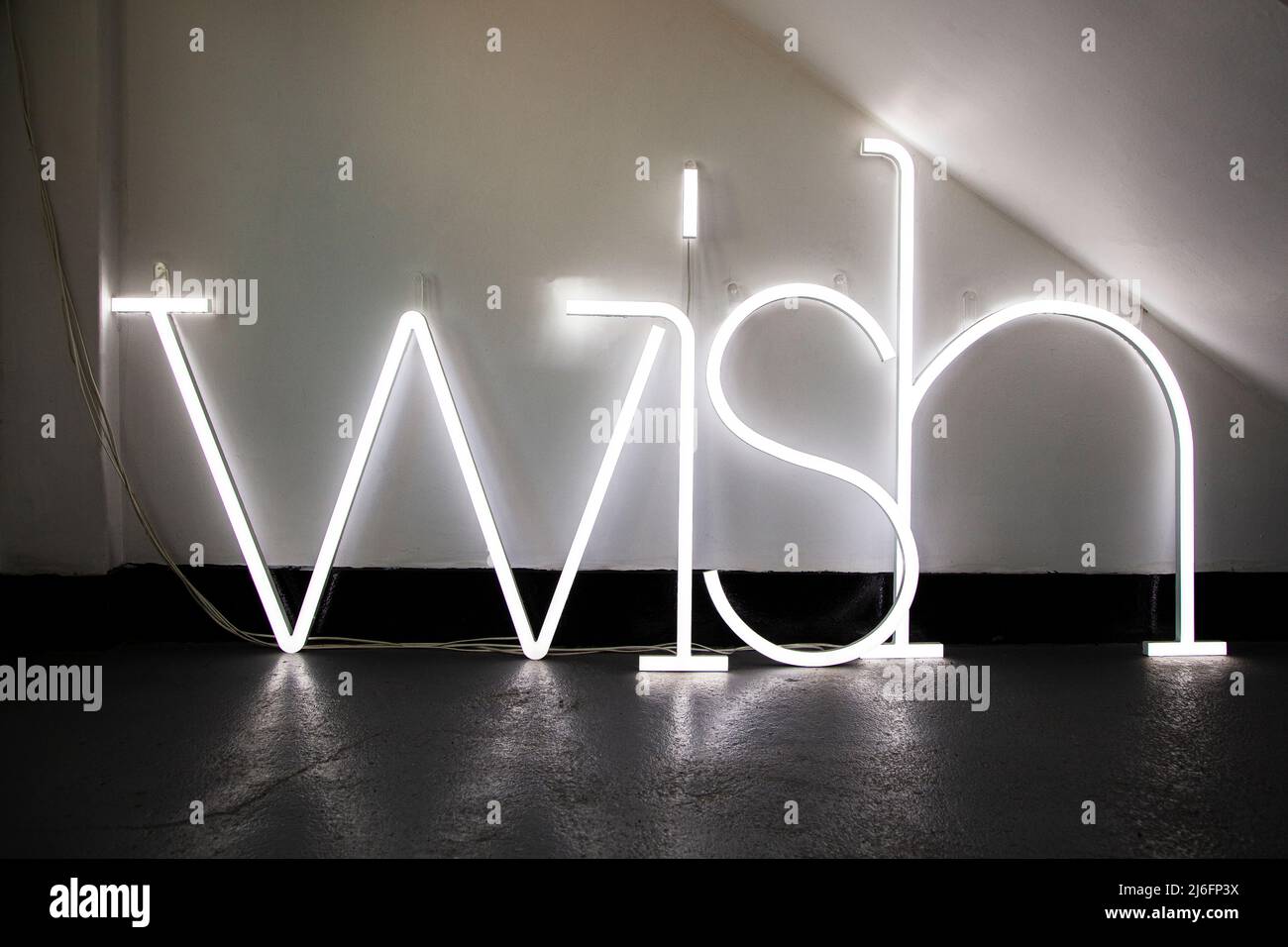 A large 'Wish" sign in dark room with white walls and grey flooring ...