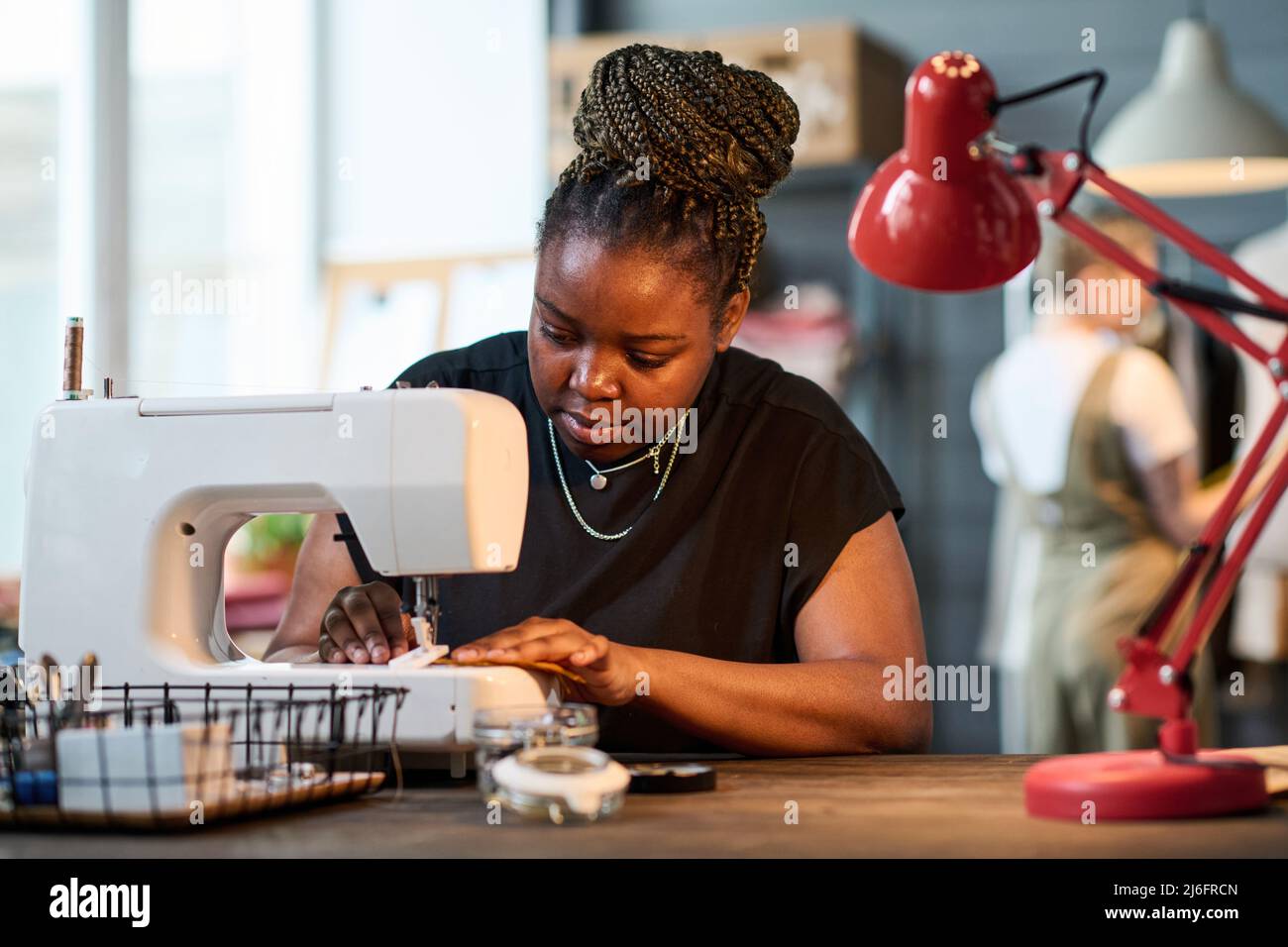 Young serious female tailor using electric sewing machine by her ...