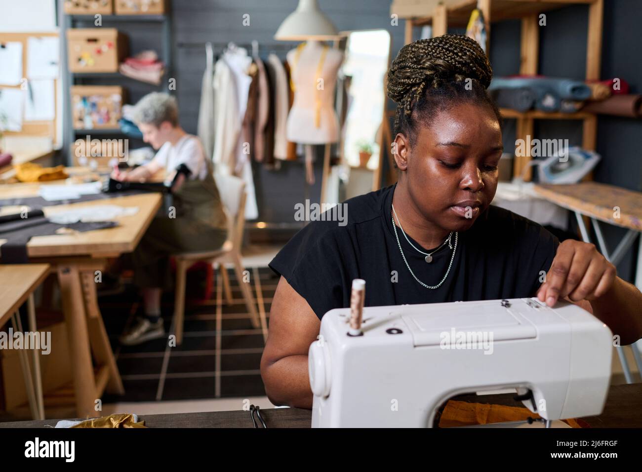 Young African American seamstress sitting by workplace in front of ...