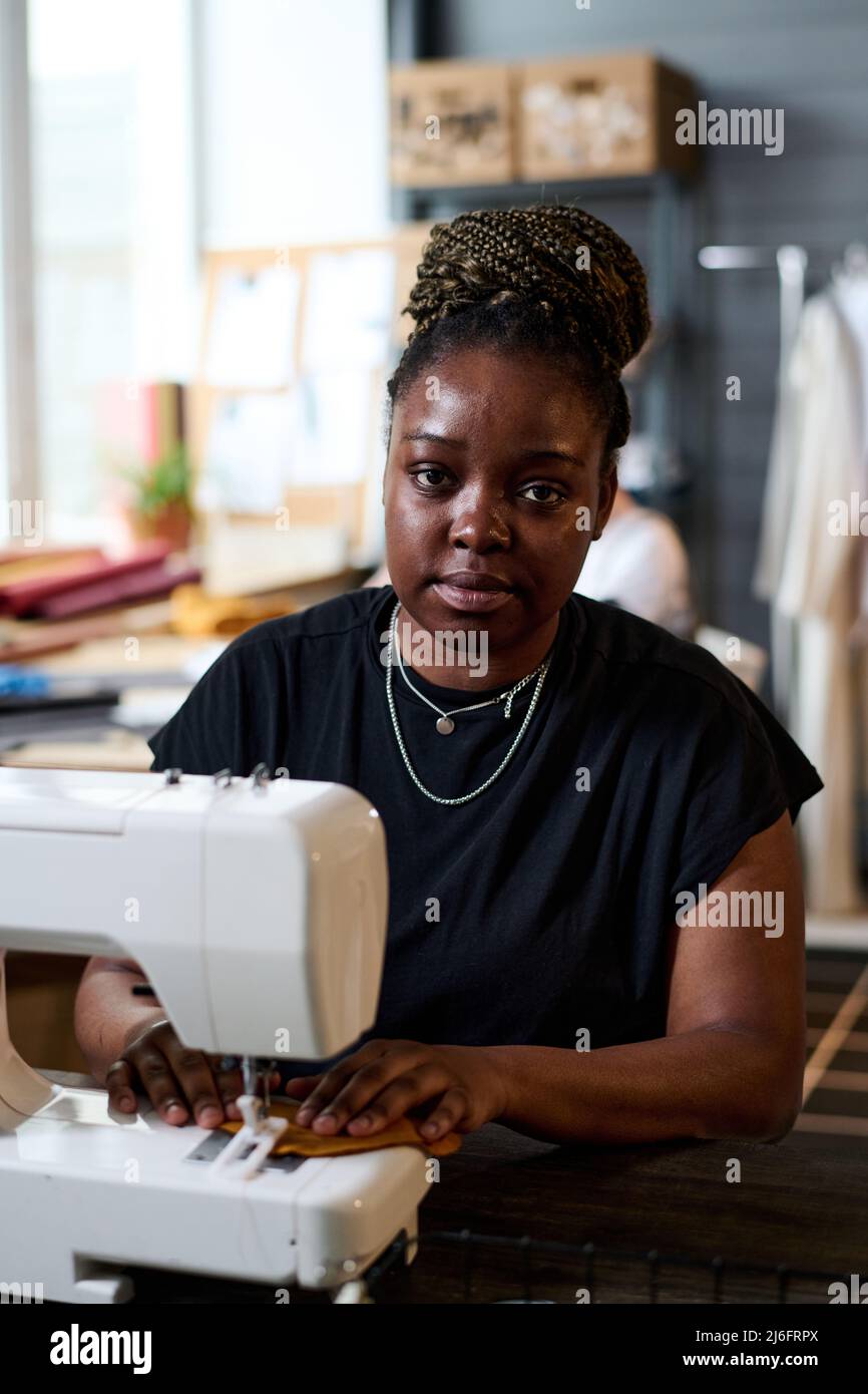 Young black woman looking at camera while sitting by workplace and ...
