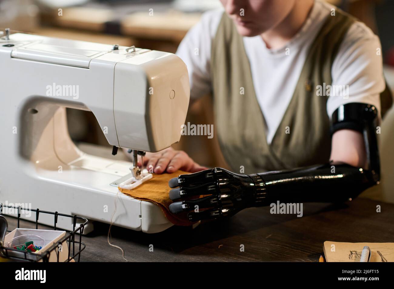 Close-up of young female with myoelectric arm prosthesis sewing clothes ...