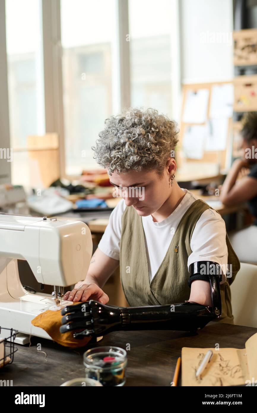 Contemporary young woman with disability working by electric sewing ...
