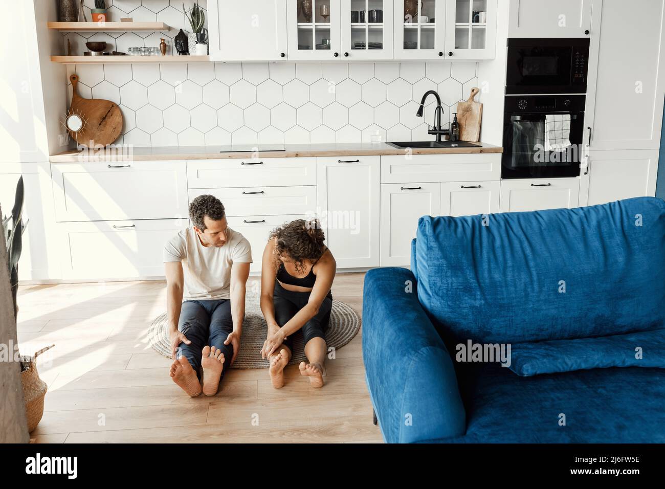 Couple exercising together on the modern kitchen floor. Man and woman in sports wear doing ...