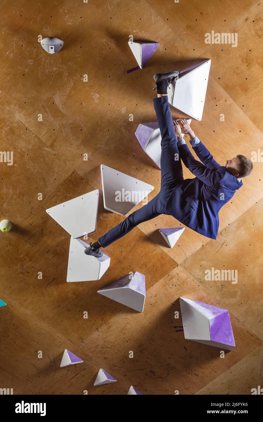 Young man in suit climbing difficult route on artificial wall in ...