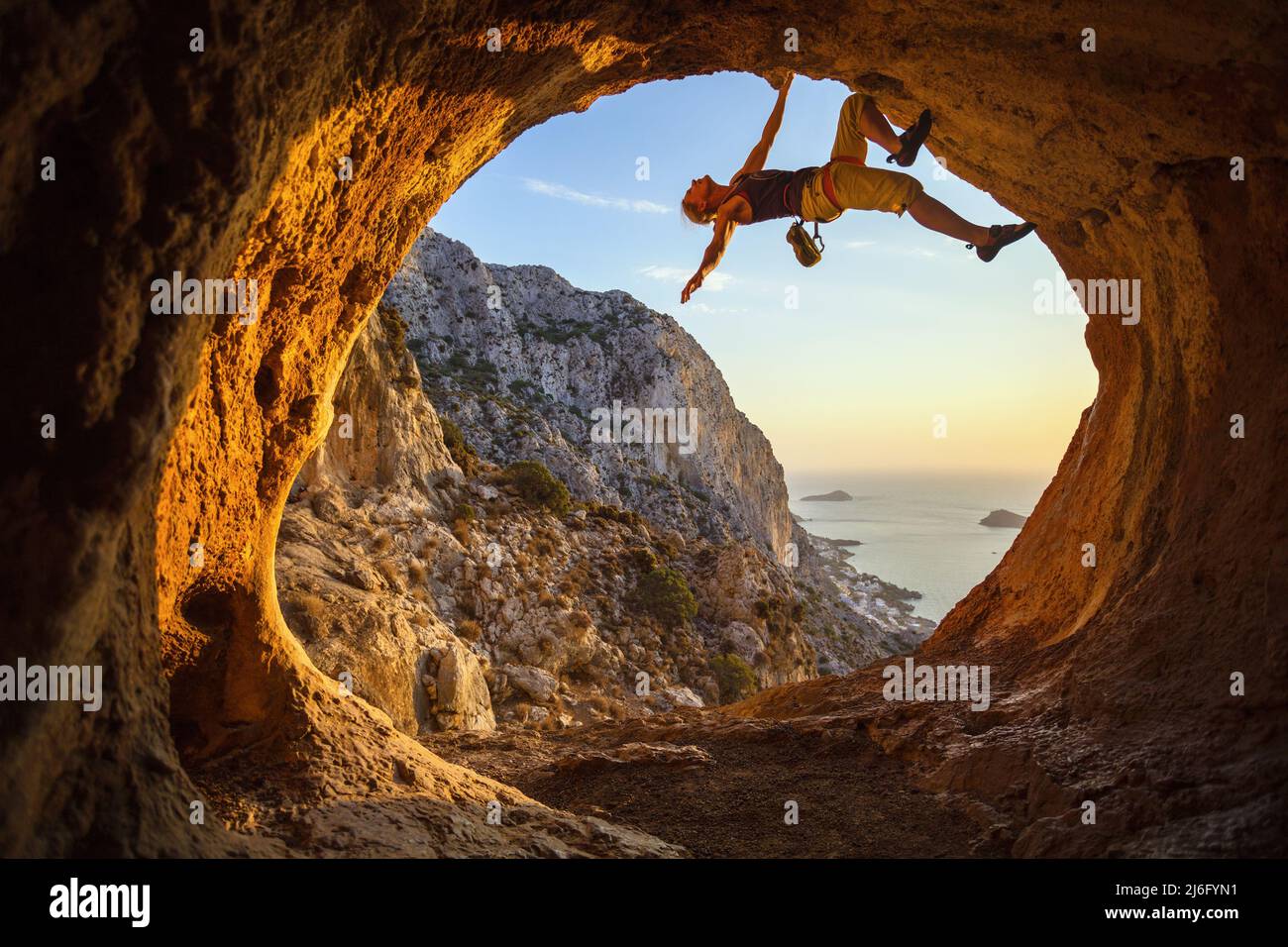 Young woman climbing in cave with beautiful sea view in background ...